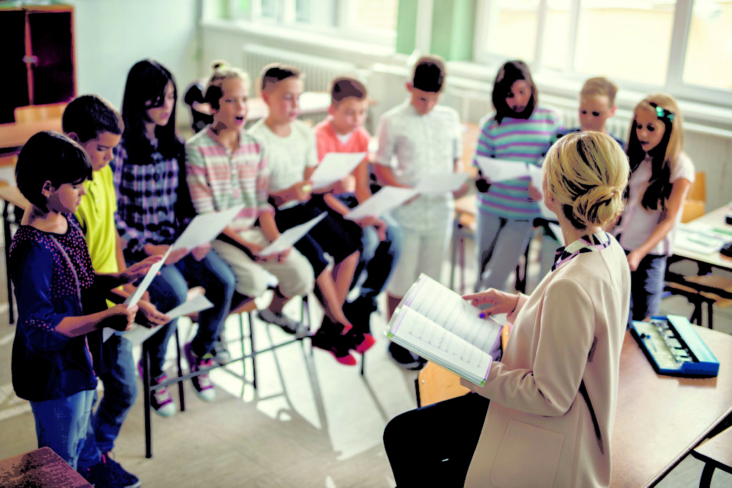 Elementary school teacher singing with children in the classroom ...